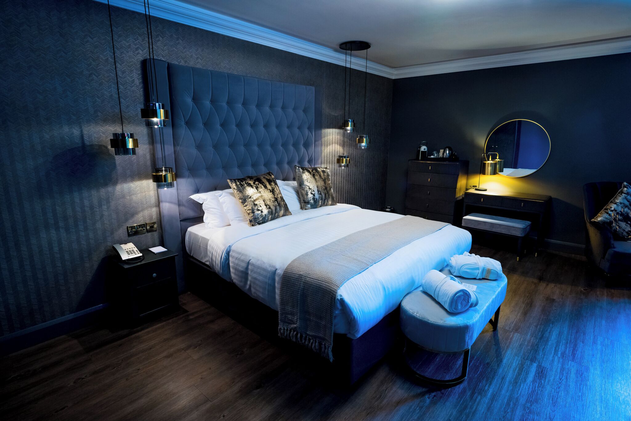 Quarto de hotel moderno com uma cama grande, mesas de cabeceira, um banco, um espelho e um guarda-roupa.
