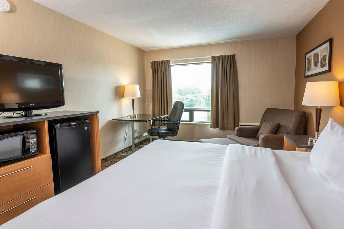 Quarto de hotel com cama, escrivaninha, cadeira, televisão e minibar.