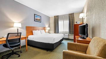 Quarto de hotel com cama, escrivaninha, cadeira, televisão e cortinas.