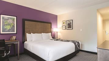 Quarto de hotel com uma cama grande, uma escrivaninha e uma cadeira. Há três quadros na parede.