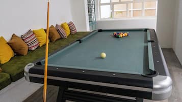 Uma mesa de bilhar com uma bola, taco de bilhar e um sofá com almofadas.