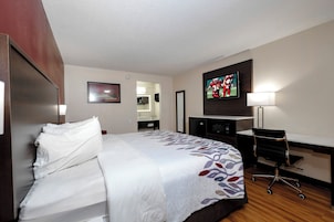 Quarto de hotel com cama, escrivaninha, televisão e uma cadeira.