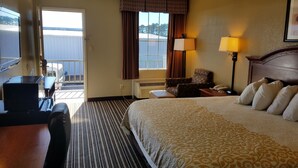 Quarto de hotel com uma cama grande, escrivaninha, cadeira, abajur e vista para o exterior.