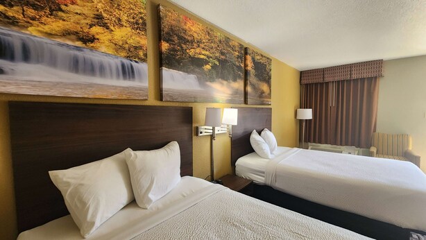 Quarto de hotel com duas camas, cabeceira, luminárias fixadas na parede e uma grande pintura de uma cachoeira.