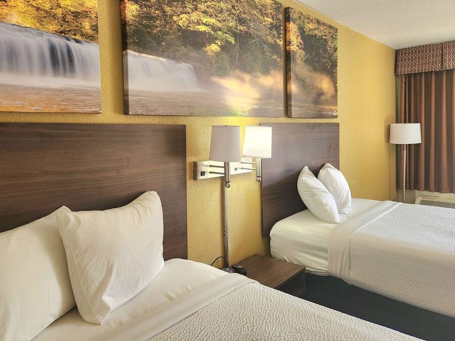 Quarto de hotel com duas camas, uma mesinha de cabeceira, um abajur e um quadro de uma cascata.