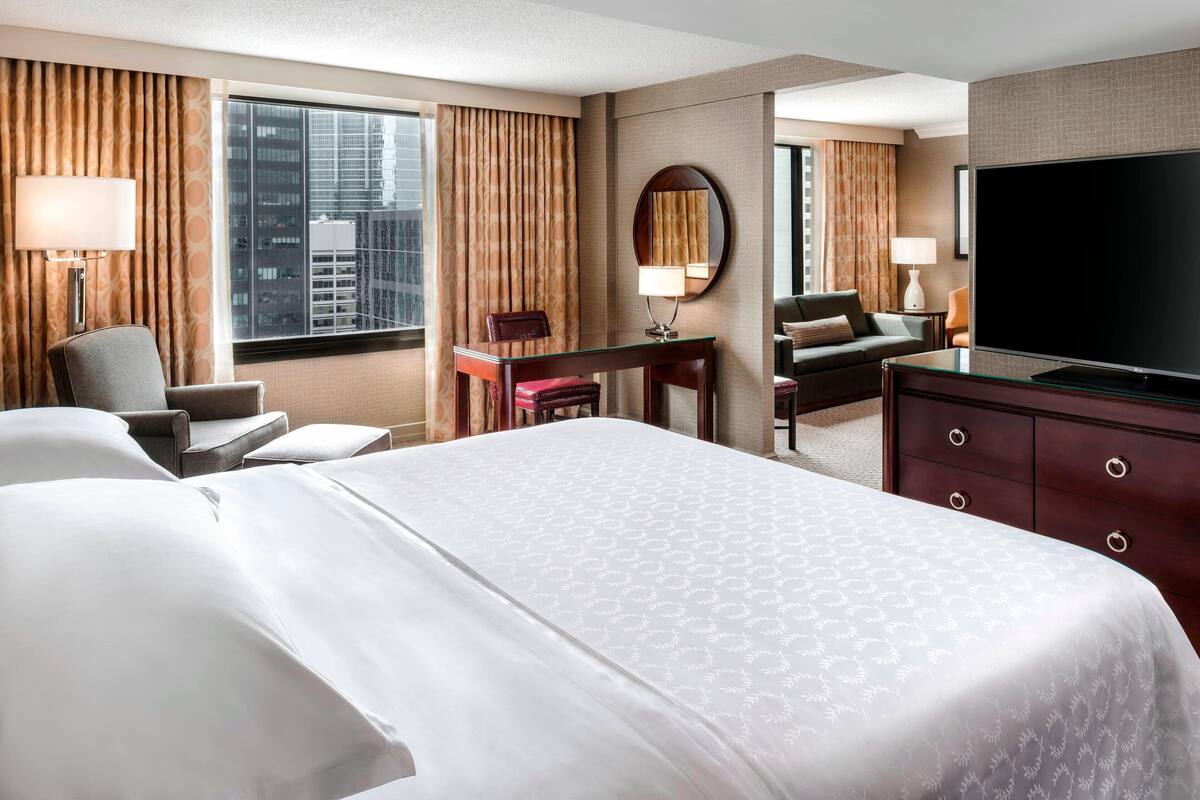 Quarto de hotel com uma cama grande, uma mesa, uma cadeira, uma televisão e vista para a cidade.