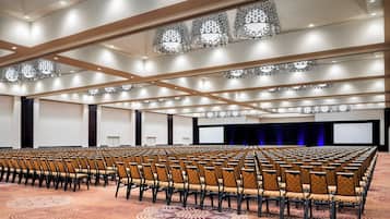 Uma sala de conferência com fileiras de cadeiras, uma tela grande e um palco.