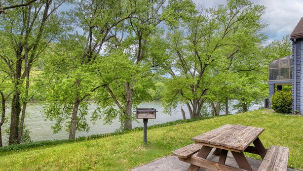 Uma mesa de piquenique perto de um lago, com árvores e um edifício ao fundo.