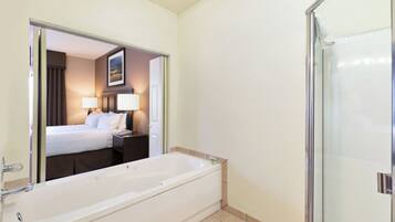 Casa de banho de hotel com banheira, chuveiro e uma cama visível por uma porta.