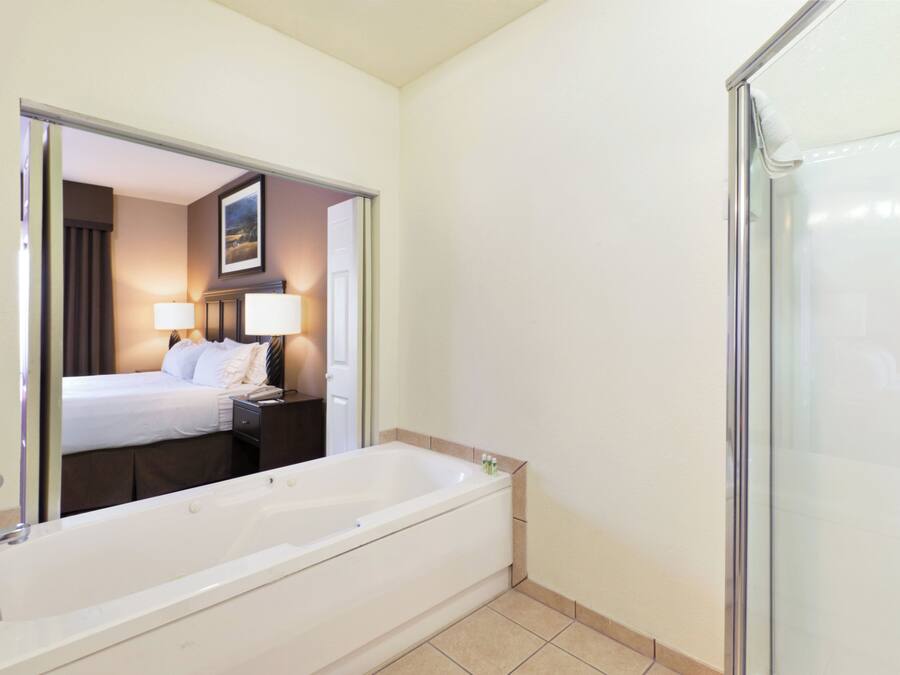 Casa de banho de hotel com banheira, chuveiro e uma cama visível por uma porta.