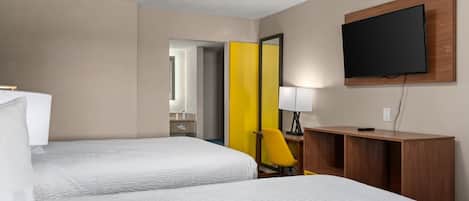 Quarto de hotel com duas camas, uma televisão presa na parede, uma secretária com cadeira e um espelho.
