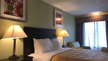 Quarto de hotel com cama, duas luminárias de cabeceira, mesa de cabeceira, encosto da cama e duas imagens emolduradas na parede.