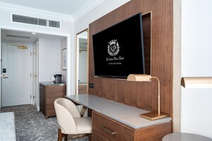 Quarto de hotel moderno com televisão de tela plana fixada numa parede de madeira, uma escrivaninha com cadeira e uma pequena mesa redonda.