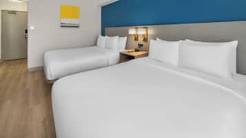 Quarto de hotel com duas camas, uma mesa de cabeceira com abajur e uma porta.