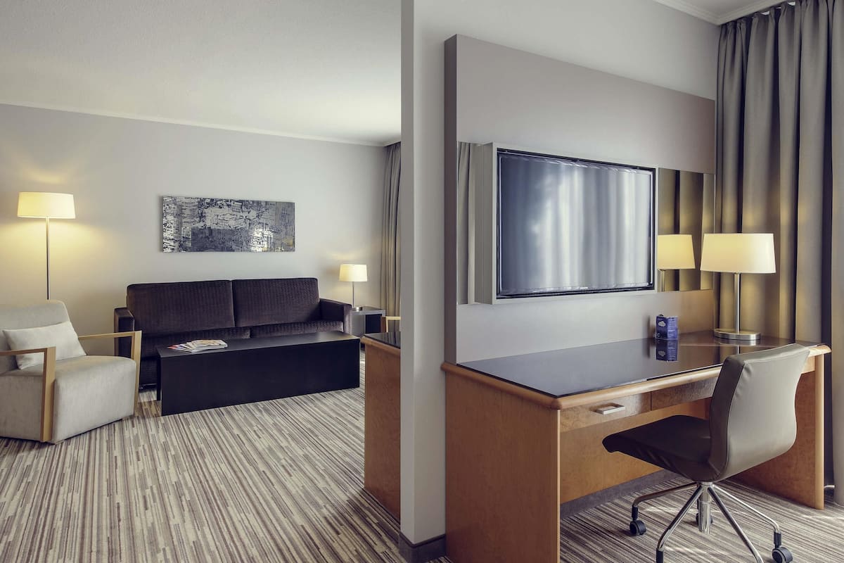 Quarto de hotel com cama, escrivaninha, cadeira, televisão e duas luminárias.