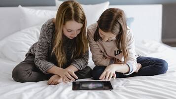 Duas pessoas sentadas em uma cama com um tablet à frente.