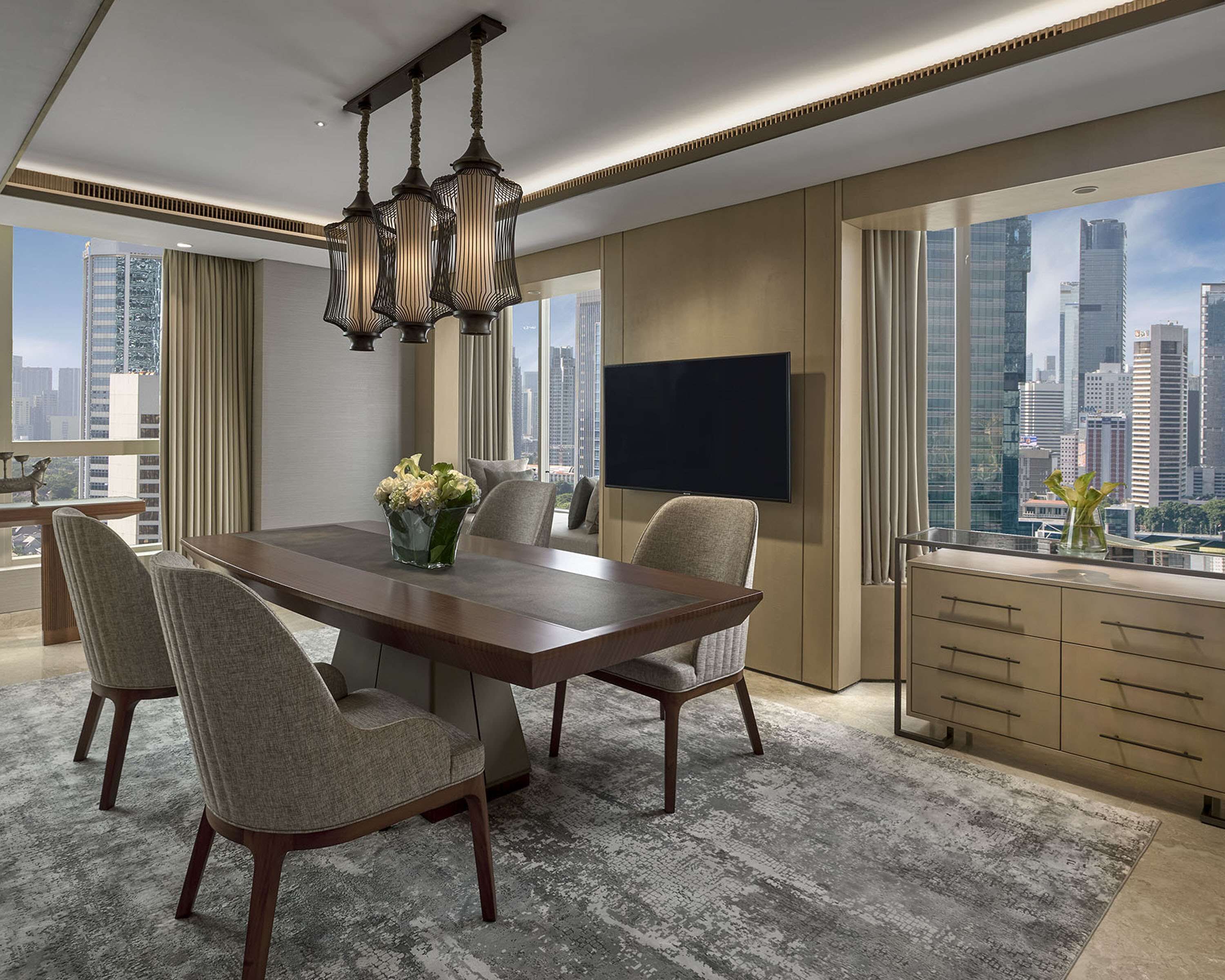 Quarto de hotel moderno com uma grande mesa de jantar, cadeiras confortáveis, televisão de tela plana e vista para a cidade.