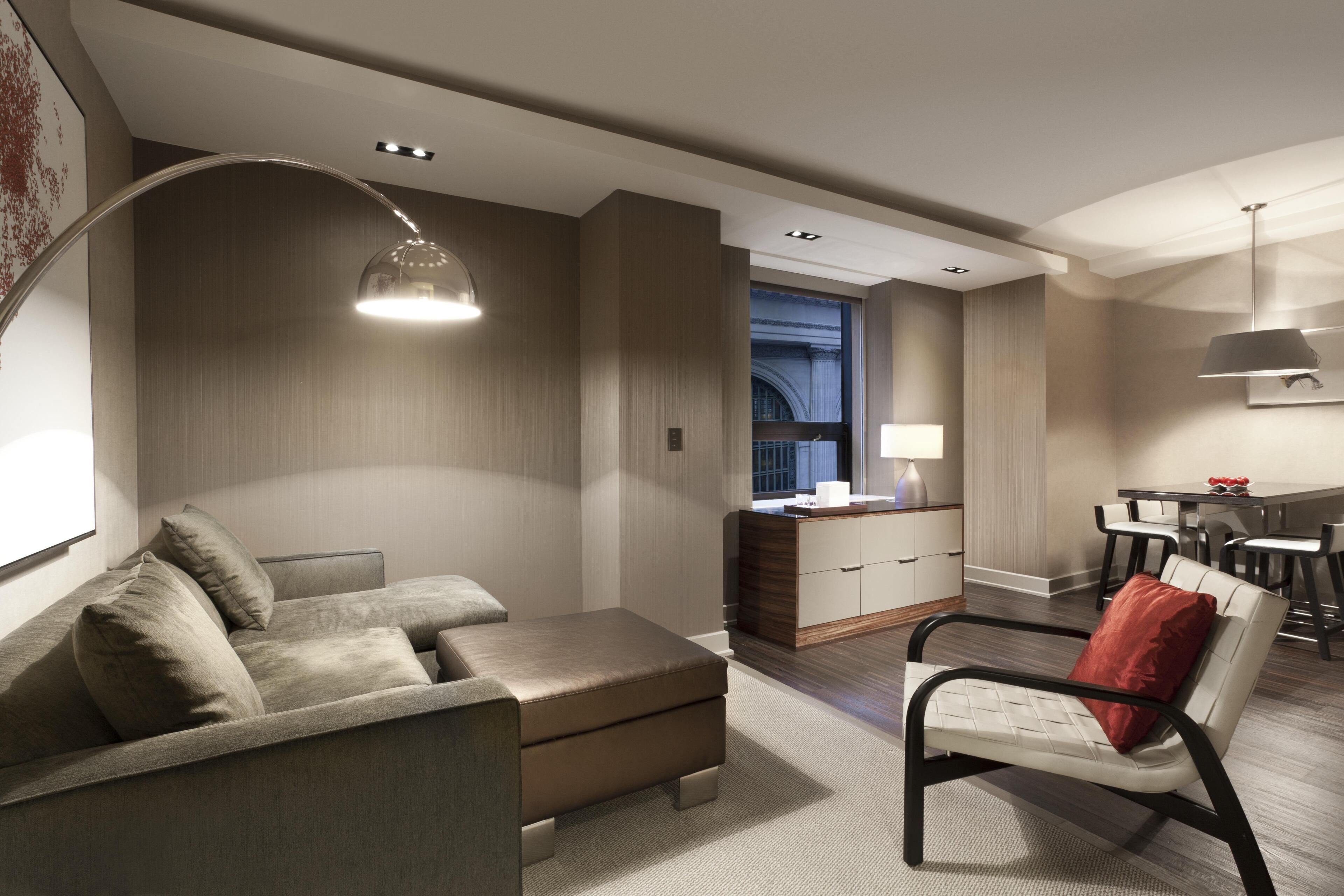 Quarto de hotel moderno com sofá, cadeira, mesa de escritório e área de refeições.