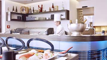 Um bar de sushi com diversos pratos de sushi, um bule de chá e um chef ao fundo.