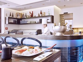 Um bar de sushi com diversos pratos de sushi, um bule de chá e um chef ao fundo.