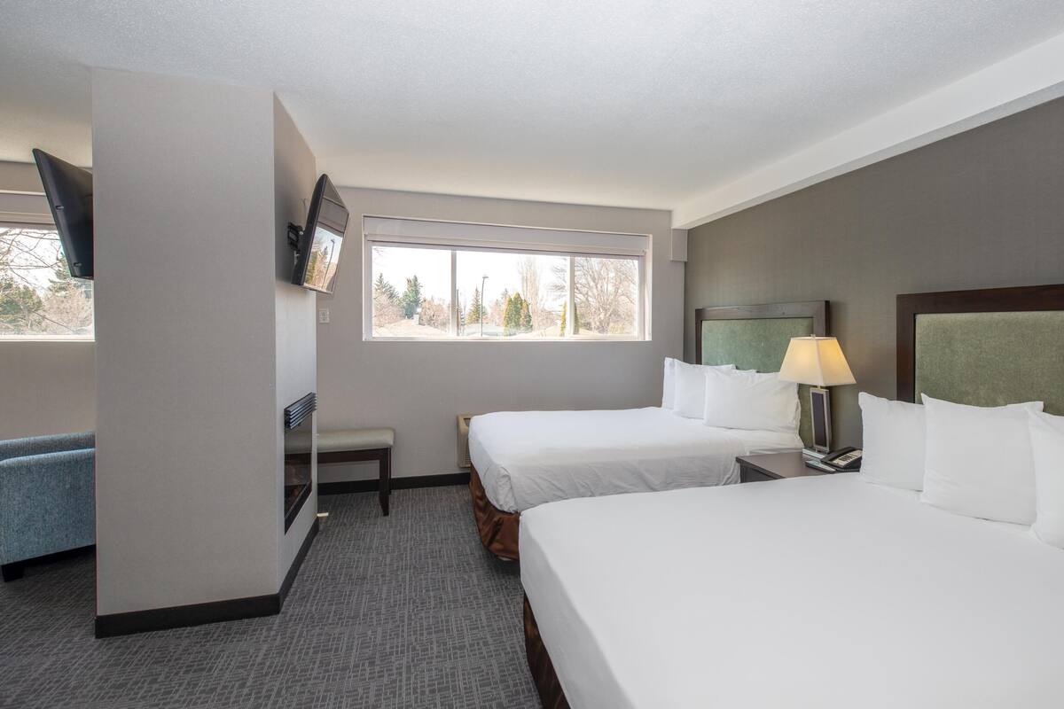 Quarto de hotel com duas camas, televisão, escrivaninha e janela com vista para árvores.