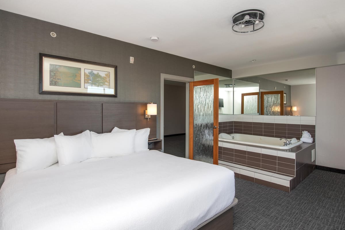 Quarto de hotel com uma cama grande, banheiro com banheira e um quadro na parede.