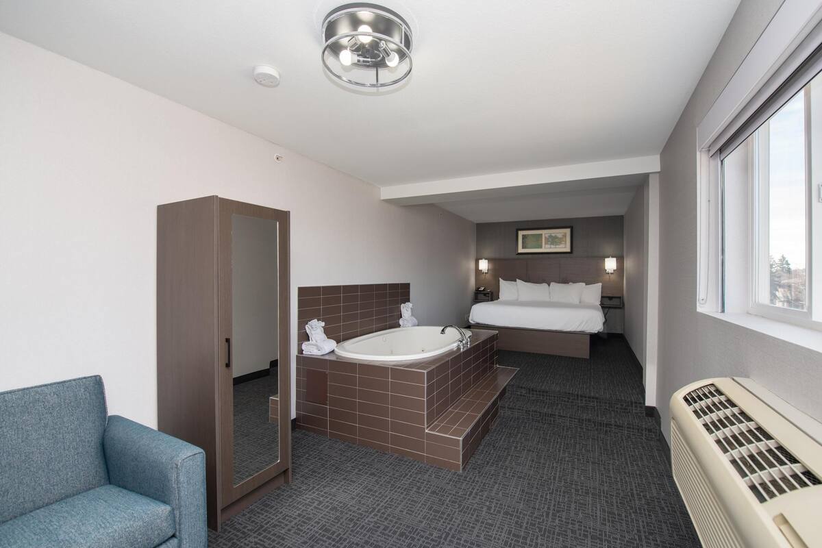 Quarto de hotel com uma banheira grande, uma cama, uma cadeira azul e um radiador.
