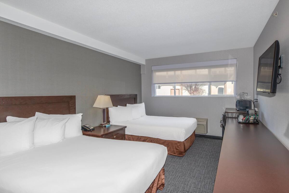 Quarto de hotel com duas camas, uma escrivaninha, luminária, televisão e janela.