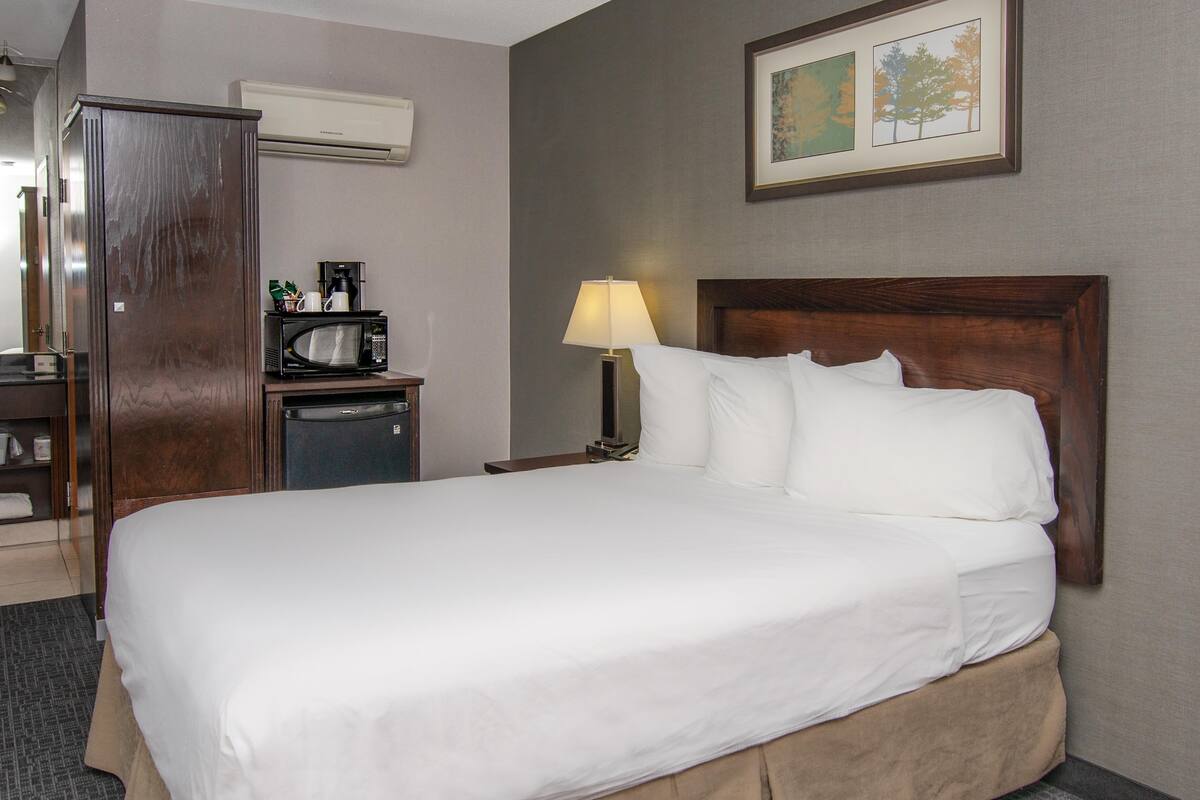Quarto de hotel com cama, escrivaninha com micro-ondas, luminária e quadro pendurado na parede.