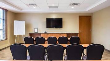 Uma sala de conferências com uma mesa comprida, cadeiras pretas, um quadro branco, uma televisão de tela plana e uma porta.