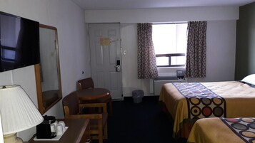 Quarto de hotel com televisão, escrivaninha com cadeira, duas camas com colchas estampadas, janela com cortinas e porta.