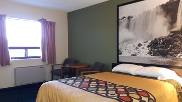Quarto de hotel com cama, janela com cortinas, uma pequena mesa com cadeira e um quadro grande de uma cascata na parede.