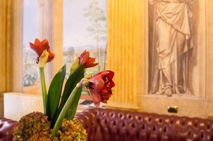 Um quarto com sofá de couro marrom, um vaso com flores vermelhas e uma estátua clássica ao fundo.