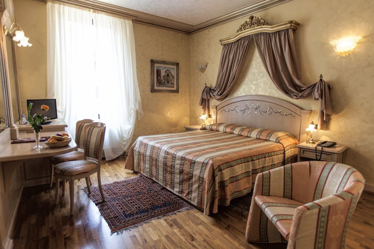 Quarto com cama grande, duas mesinhas de cabeceira, escrivaninha com cadeira, tapete e quadro na parede.