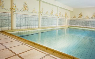 Uma grande piscina interior com paredes e chão revestidos em azulejos.