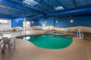 Piscina interna com espreguiçadeiras e mesas, água azul cristalina e teto alto com vigas aparentes.