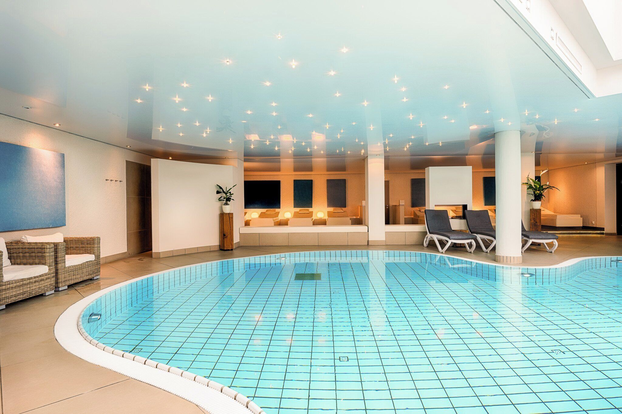 Uma grande piscina interior com espreguiçadeiras e uma área de recepção.