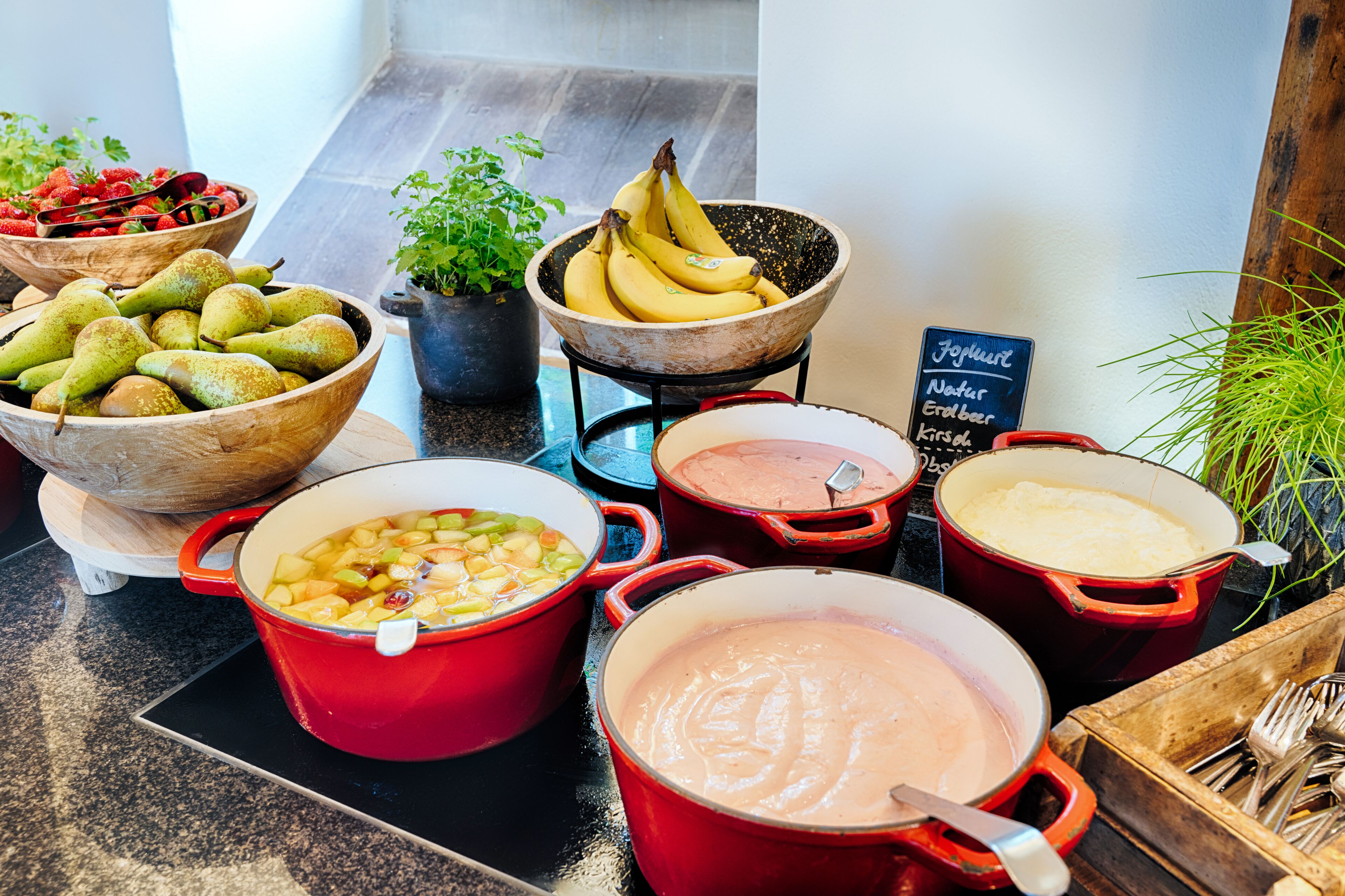 Buffet com diversas frutas, legumes e pratos em panelas vermelhas.