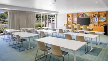 Uma sala de aula com mesas, cadeiras, um quadro negro e uma estante com diversos objetos.
