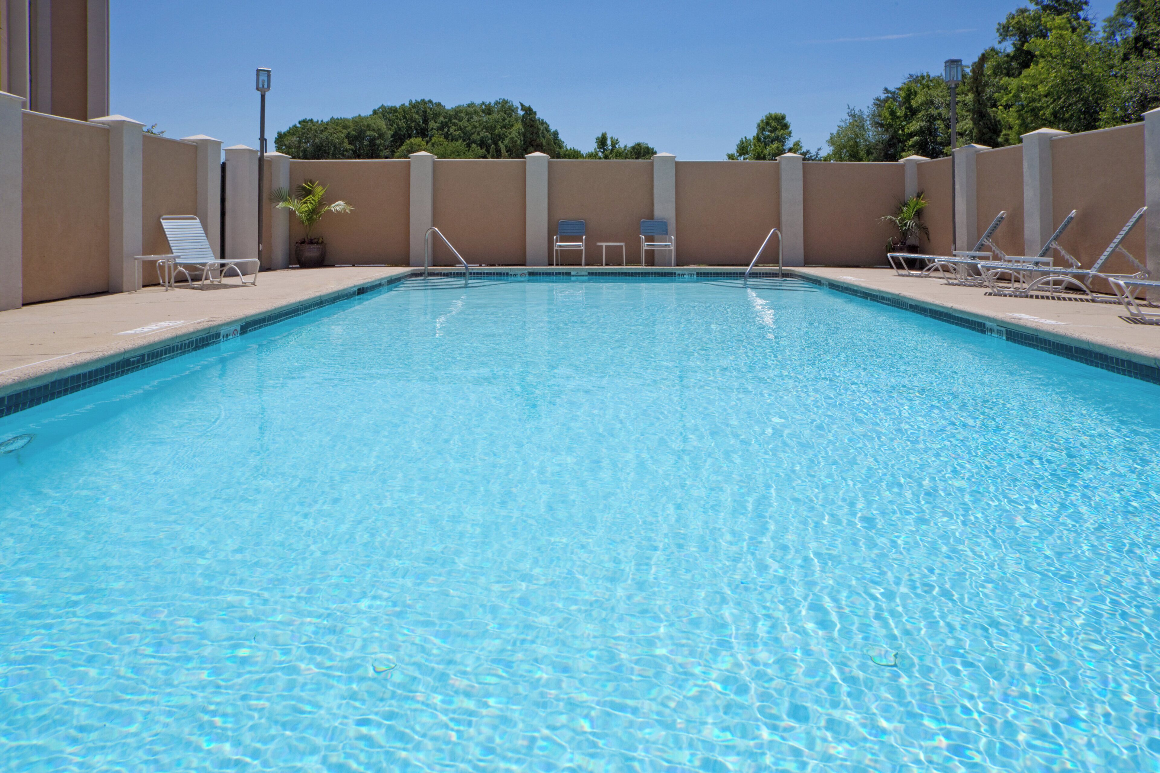 Piscina azul límpida com espreguiçadeiras e um pequeno muro.