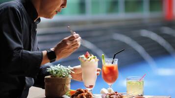 Uma pessoa jantando à mesa com vários pratos, incluindo um milkshake, um coquetel e uma refeição.