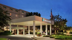 Entrada de hotel com área coberta, uma bandeira americana e uma placa com a inscrição "Embassy Suites".