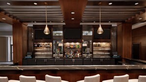 Uma área de bar moderna, com um balcão comprido, vários bancos altos e uma variedade de garrafas de bebidas e copos expostos em prateleiras.