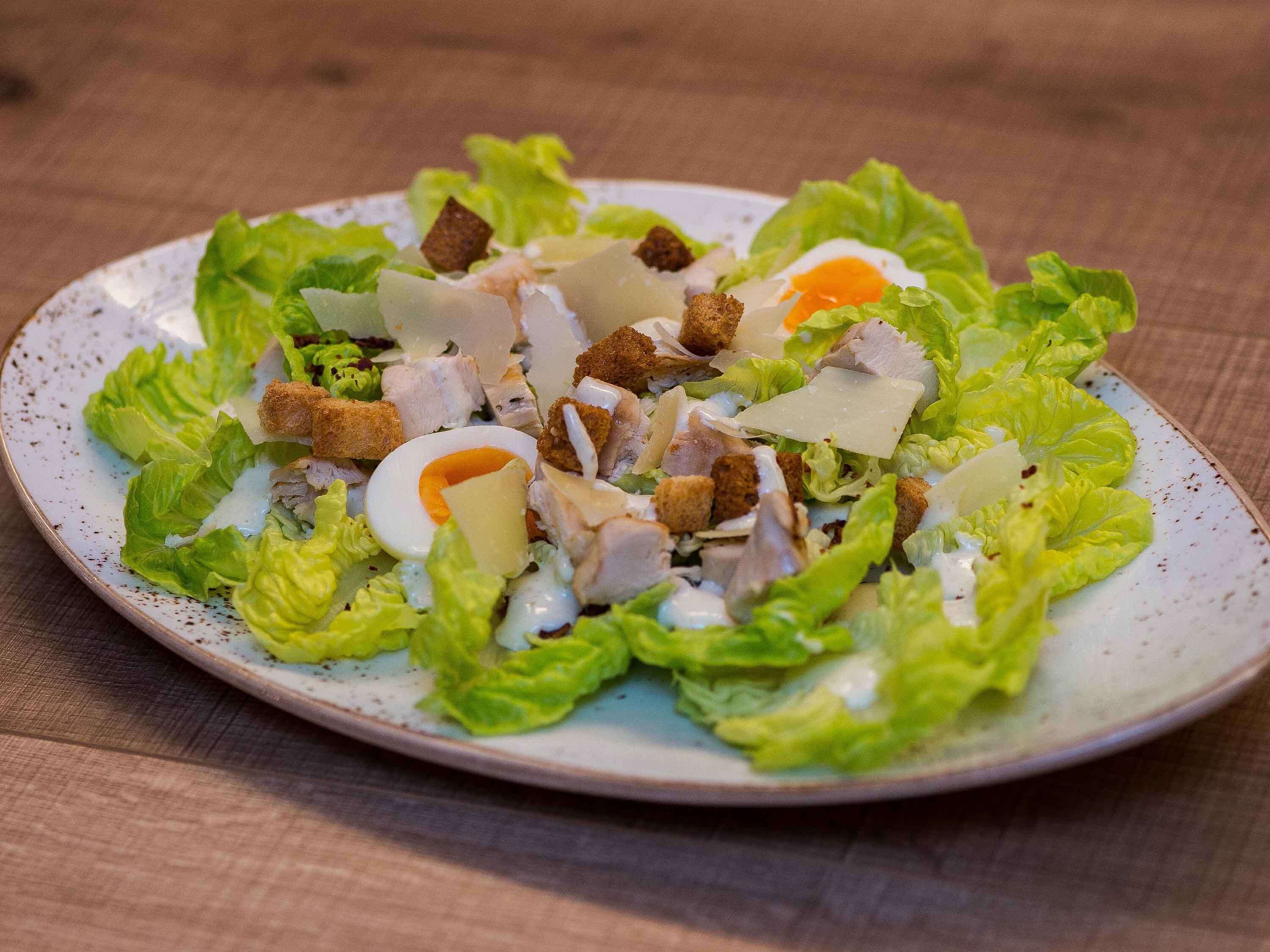 Uma salada Caesar com alface, croutons, frango, queijo e ovo cozido.