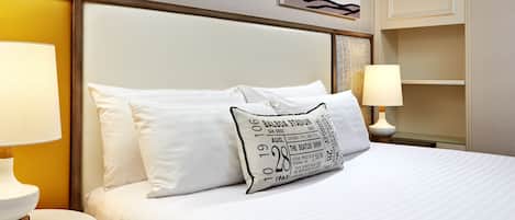 Quarto de hotel com uma cama bem arrumada, duas luminárias de cabeceira e uma obra de arte emoldurada na parede.