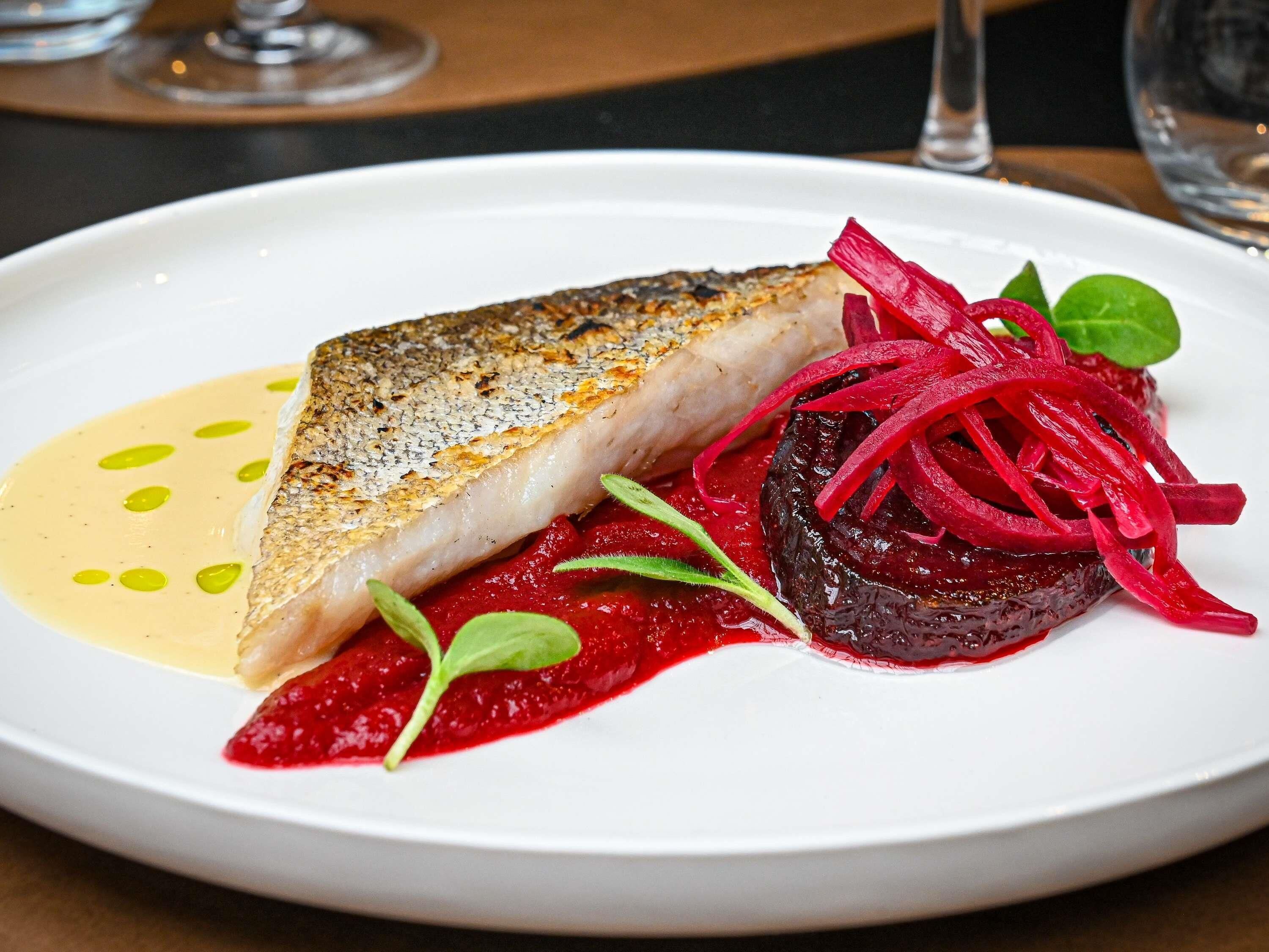 Um prato branco com um pedaço de peixe, beterraba e vegetais.