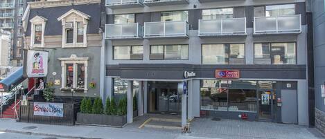 Um hotel de vários andares com varandas, fachada comercial e entrada visível.