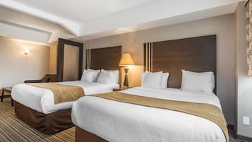 Quarto de hotel com duas camas, uma mesa, uma cadeira e um abajur.