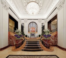 Um hall imponente com escadaria de mármore, um candelabro e arranjos florais.