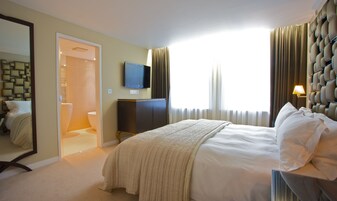 Quarto de hotel com uma cama grande, televisão presa na parede, guarda-roupa e banheiro visível por uma porta aberta.